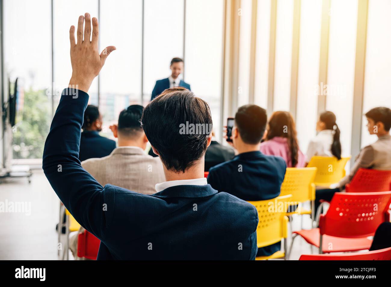 Curious individual in a diverse group raises a hand during a conference ...