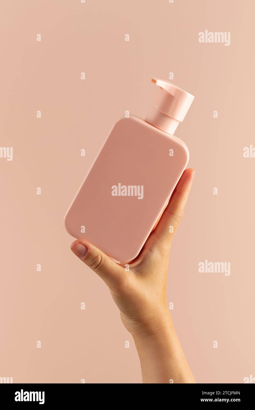 A mock-up of a pink dispenser with cosmetics in a woman's hand. A ...