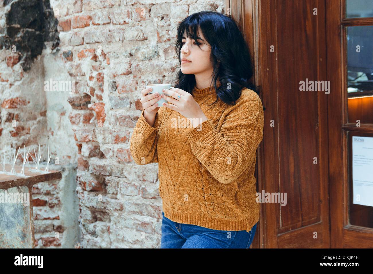 Vertical image of young Latina woman with brown sweater and blue jean ...