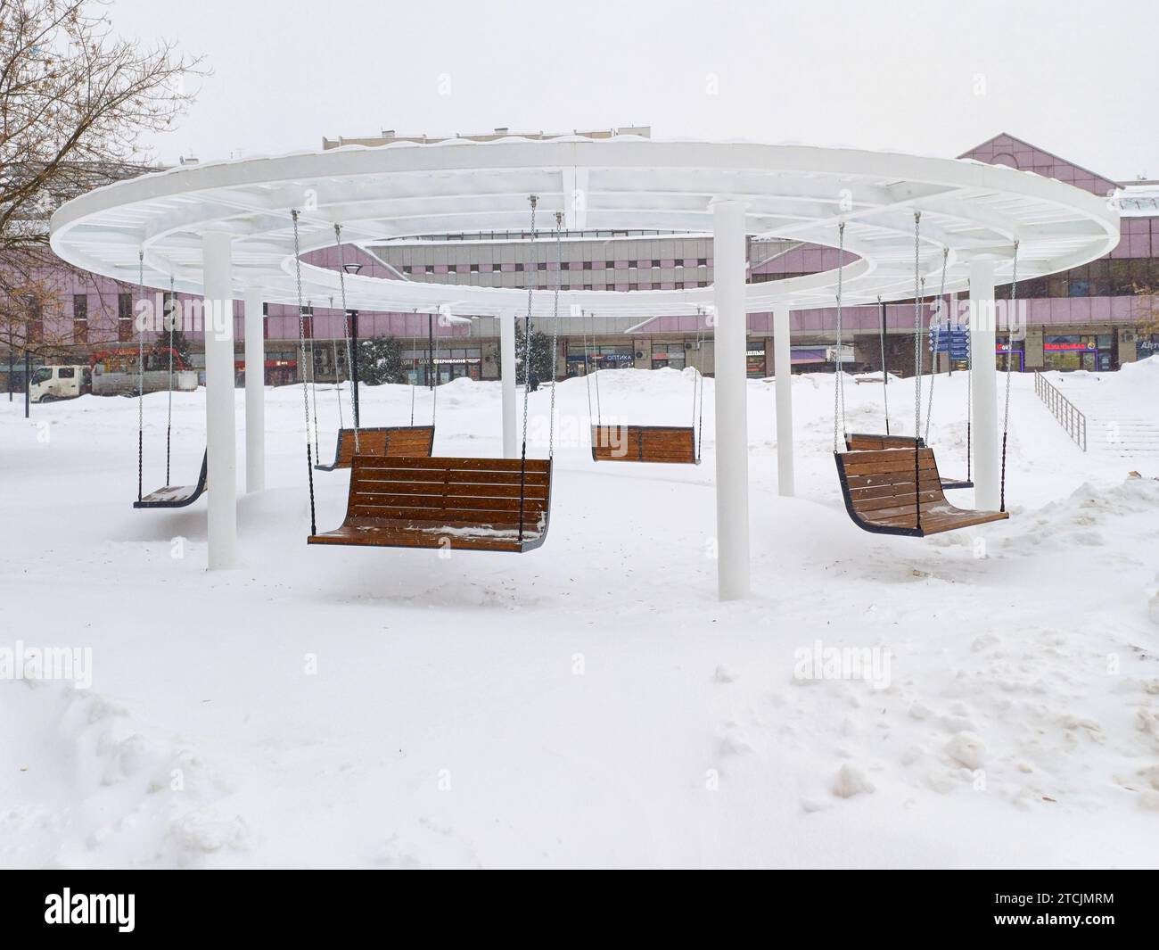 Snow-covered hanging swing in the snowfall in the city on a winter day ...