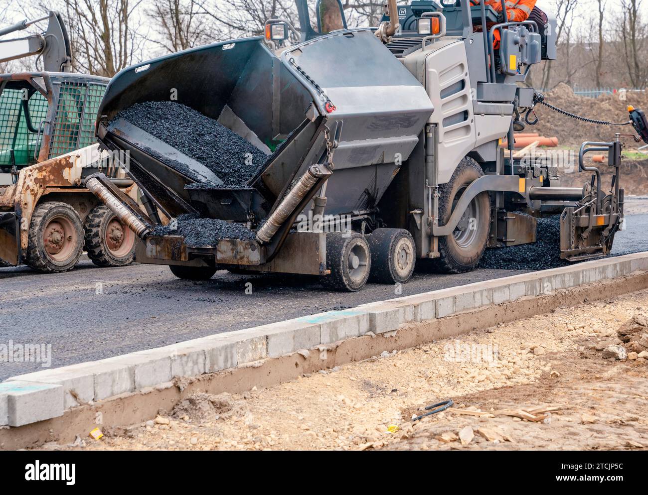 Asphalt paver filled with hot tarmac laying new road surface on new ...