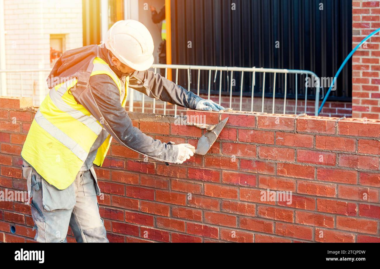 Hard working bricklayer lays bricks on cement mix on construction site ...