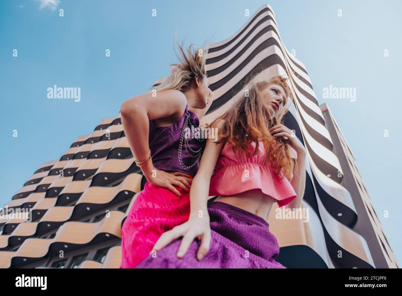 Two confident, well-dressed women striking poses against a modern ...