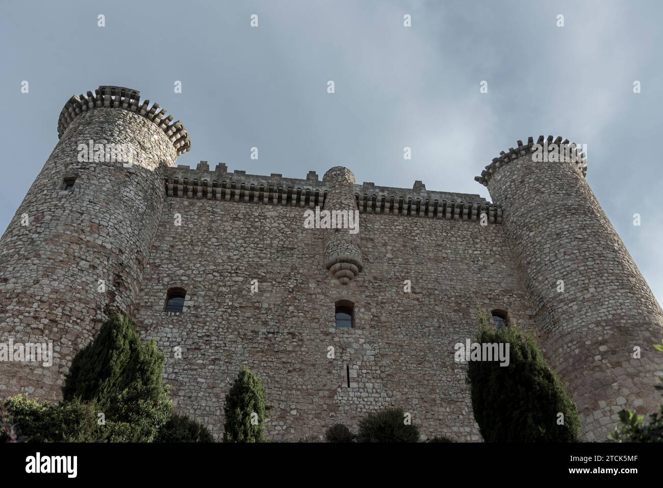 stone castle with two towers and a wall with battlements stands against ...