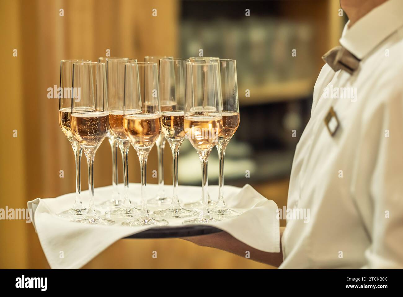 A young waiter holds a plate with champagne or prosecco as a welcome ...