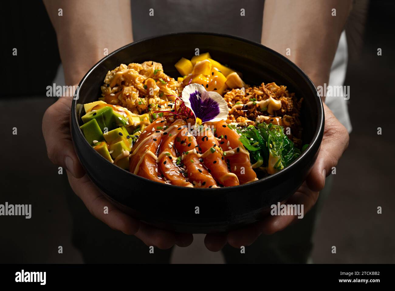A chef's hands hold a black bowl filled with a colorful arrangement of ...