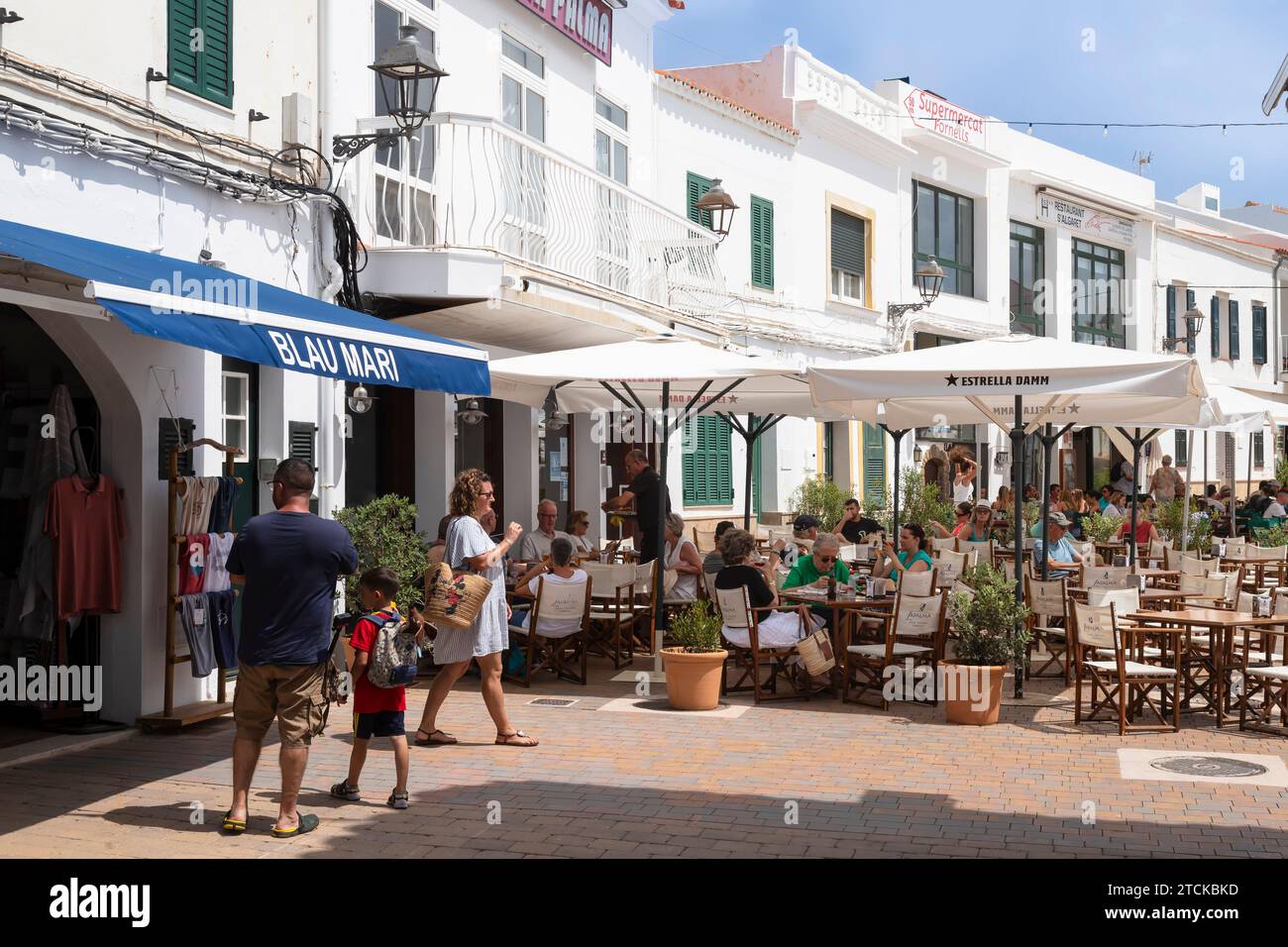 Tourists walk through a narrow cozy street with restaurants and shops ...