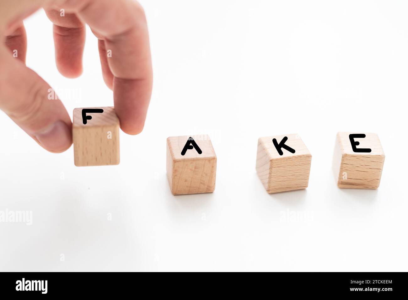 The word FAKE, spelt with wooden letter tiles, over a white background ...