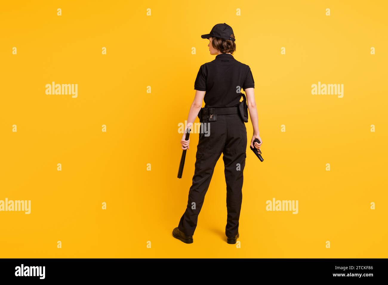 Full size rear portrait of police woman standing arms hold pistol baton ...