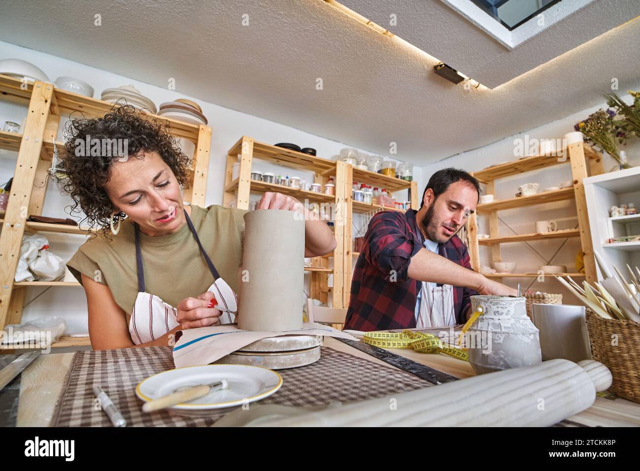 Two potters intensely focused on shaping and detailing their ceramic pieces, immersed in the ...