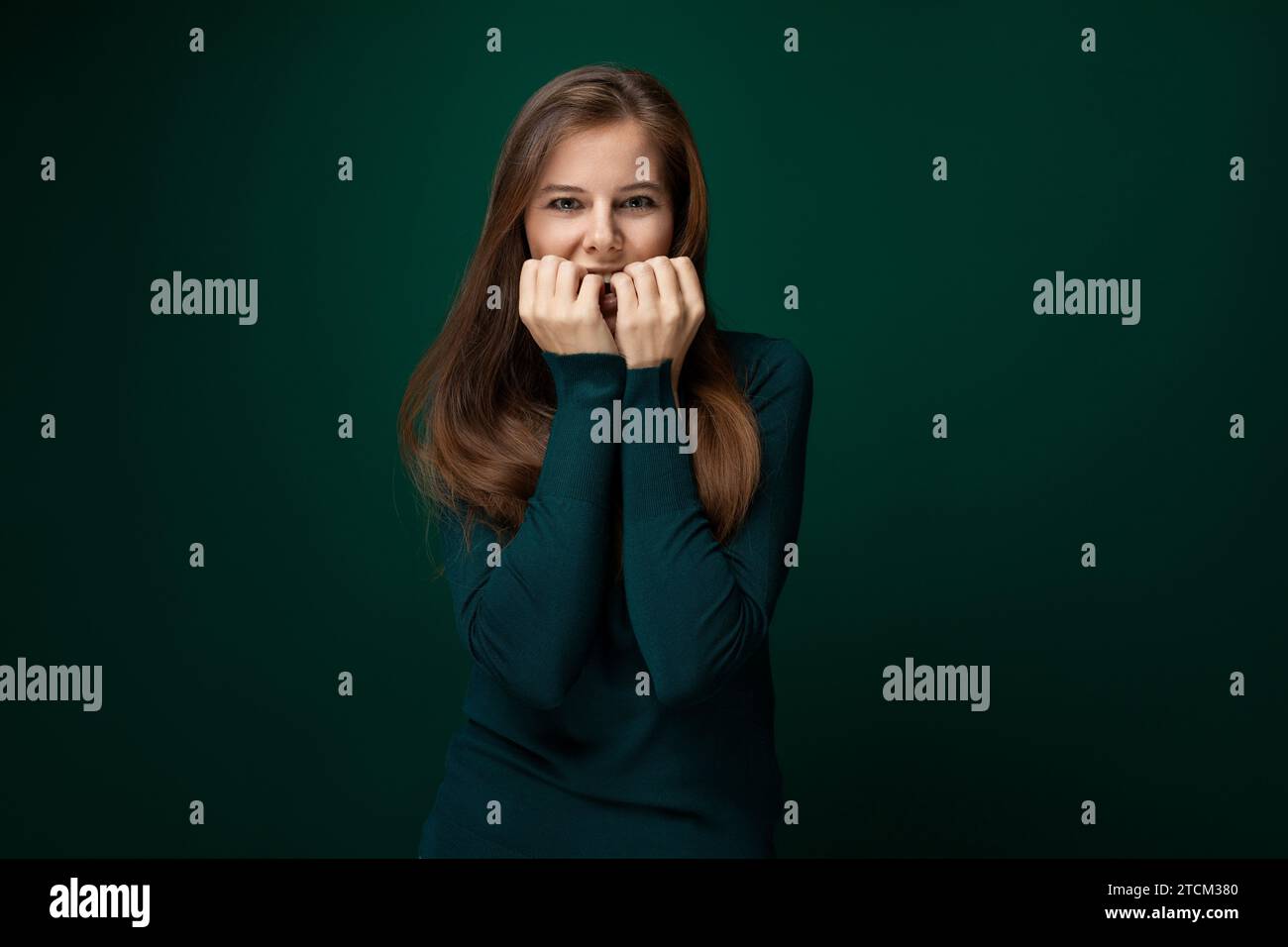 Cute modest woman with brown natural hair posing shyly on dark green ...