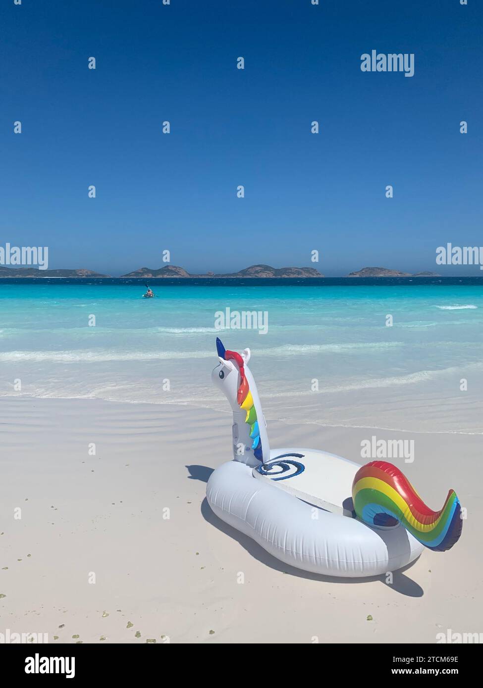 A whimsical inflatable rainbow-colored unicorn floating against a beach ...