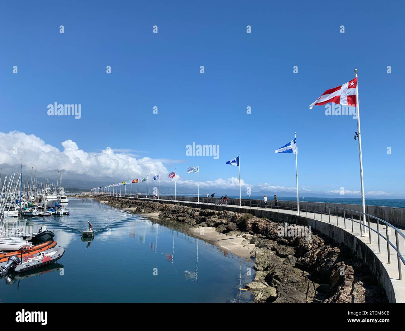 Boats are lined up along the shoreline in a sunny harbor, illuminated ...