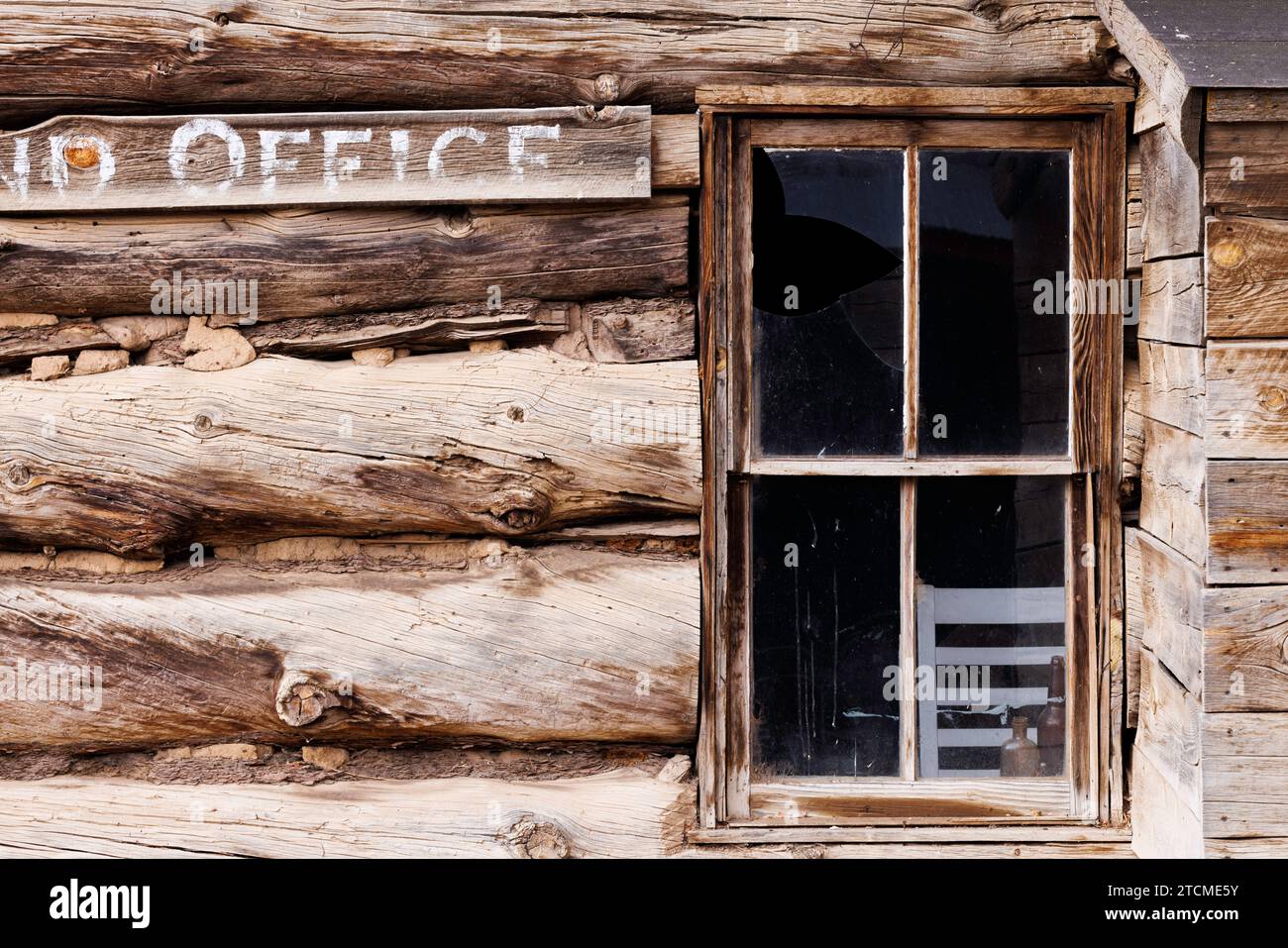 dark broken window with white chair on the wall of a log cabin with ...