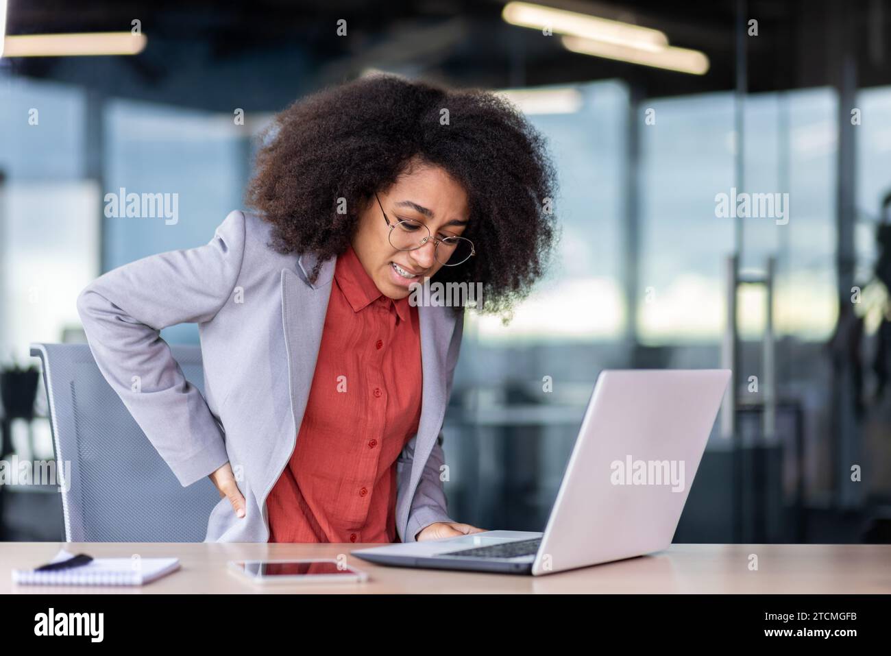 Female office worker suffers from back pain, holds her hand on her ...