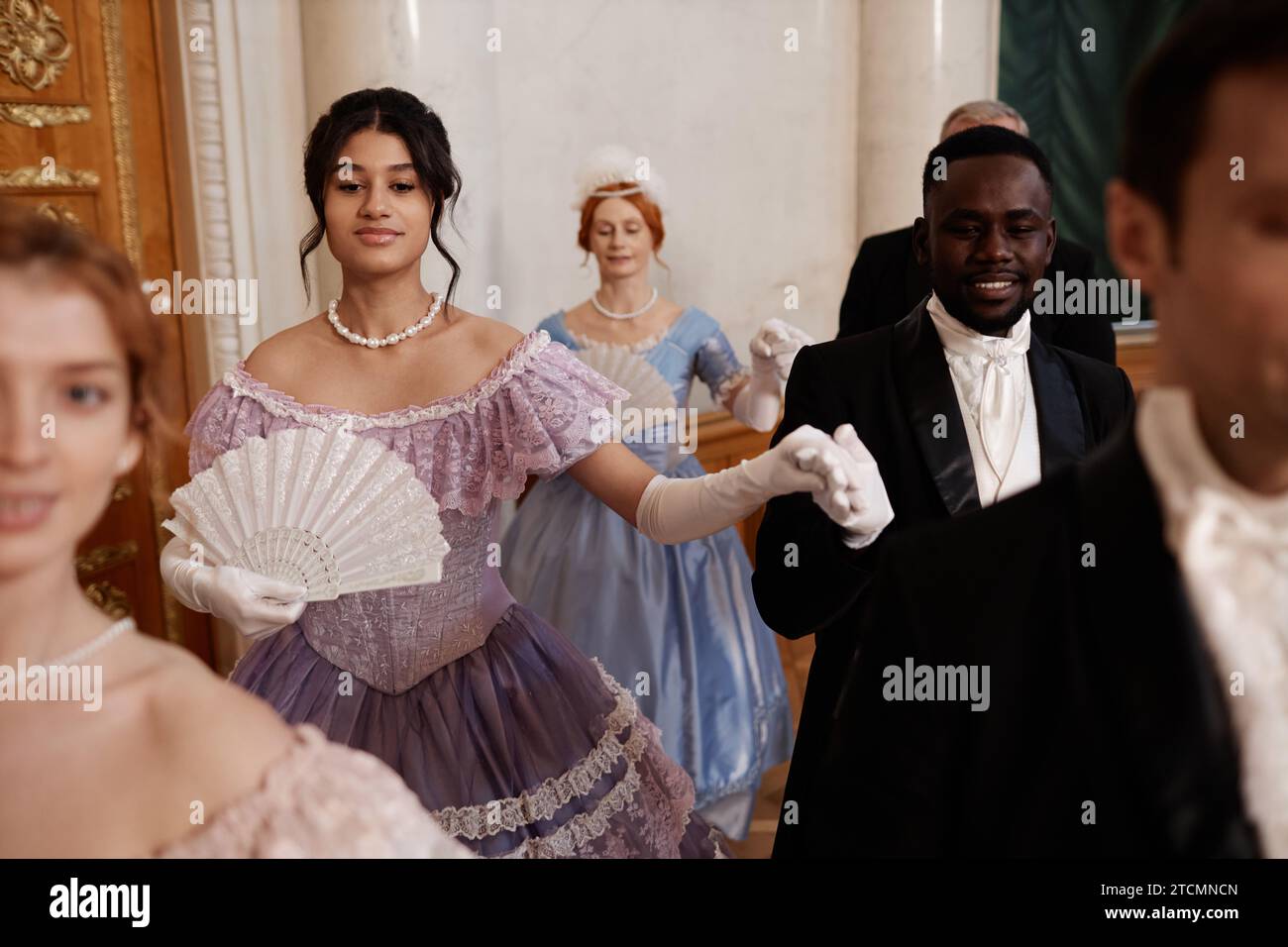 Diverse group of ladies and gentlemen enjoying dance ball in palace and ...