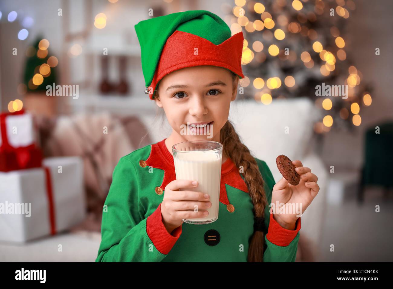 Cute little girl in elf costume drinking milk with cookie at home on ...