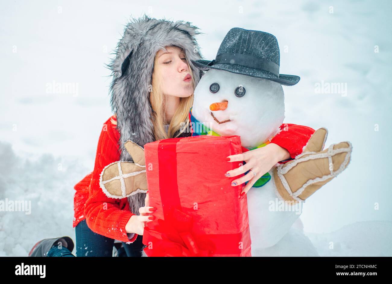 Funny snowmen. Happy smiling girl kissing snowman on sunny winter day ...