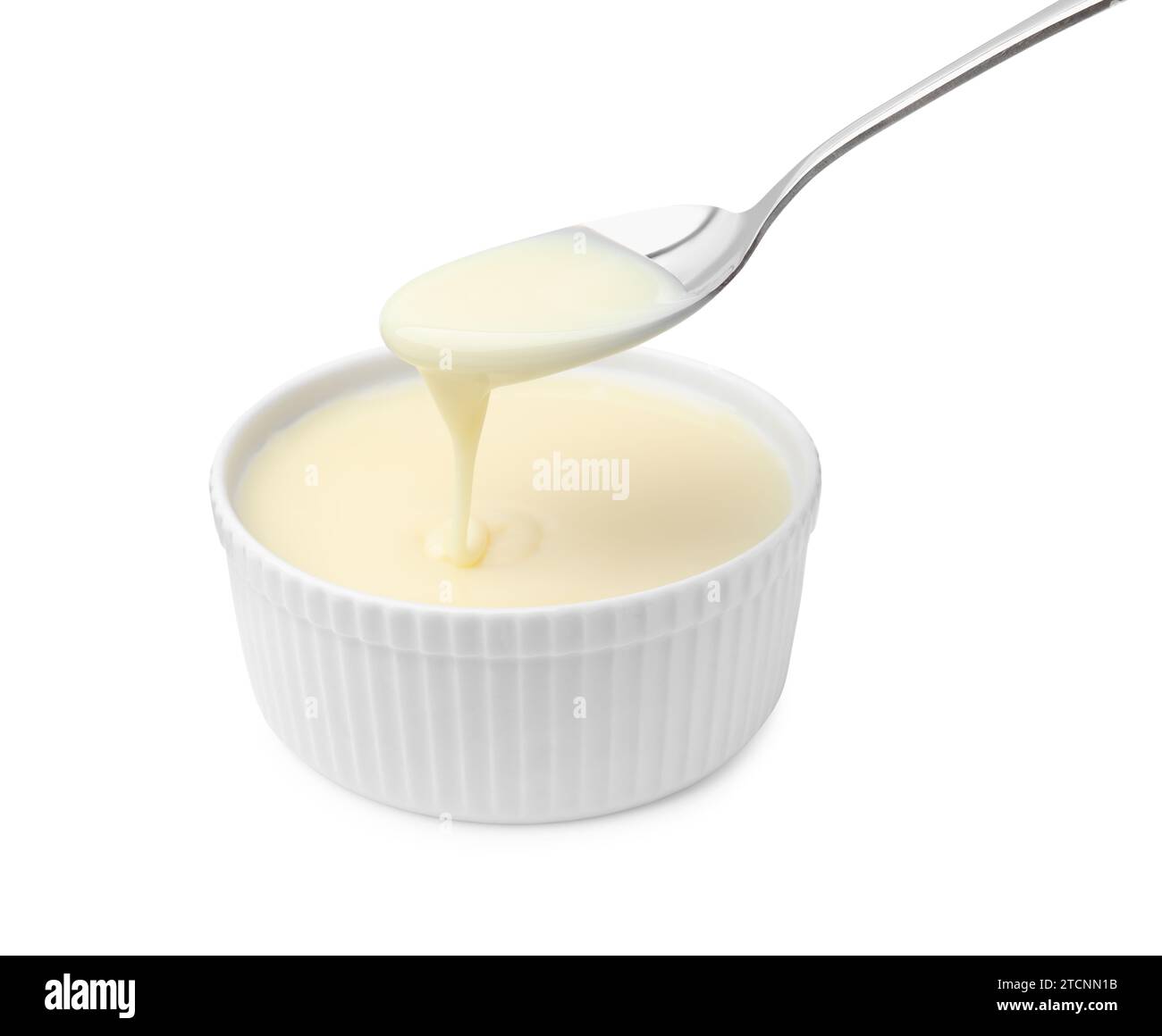 Condensed milk flowing down from spoon into bowl isolated on white ...