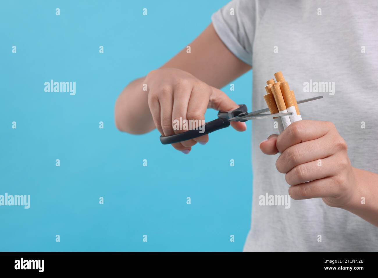 Stop smoking concept. Woman cutting cigarettes on light blue background ...