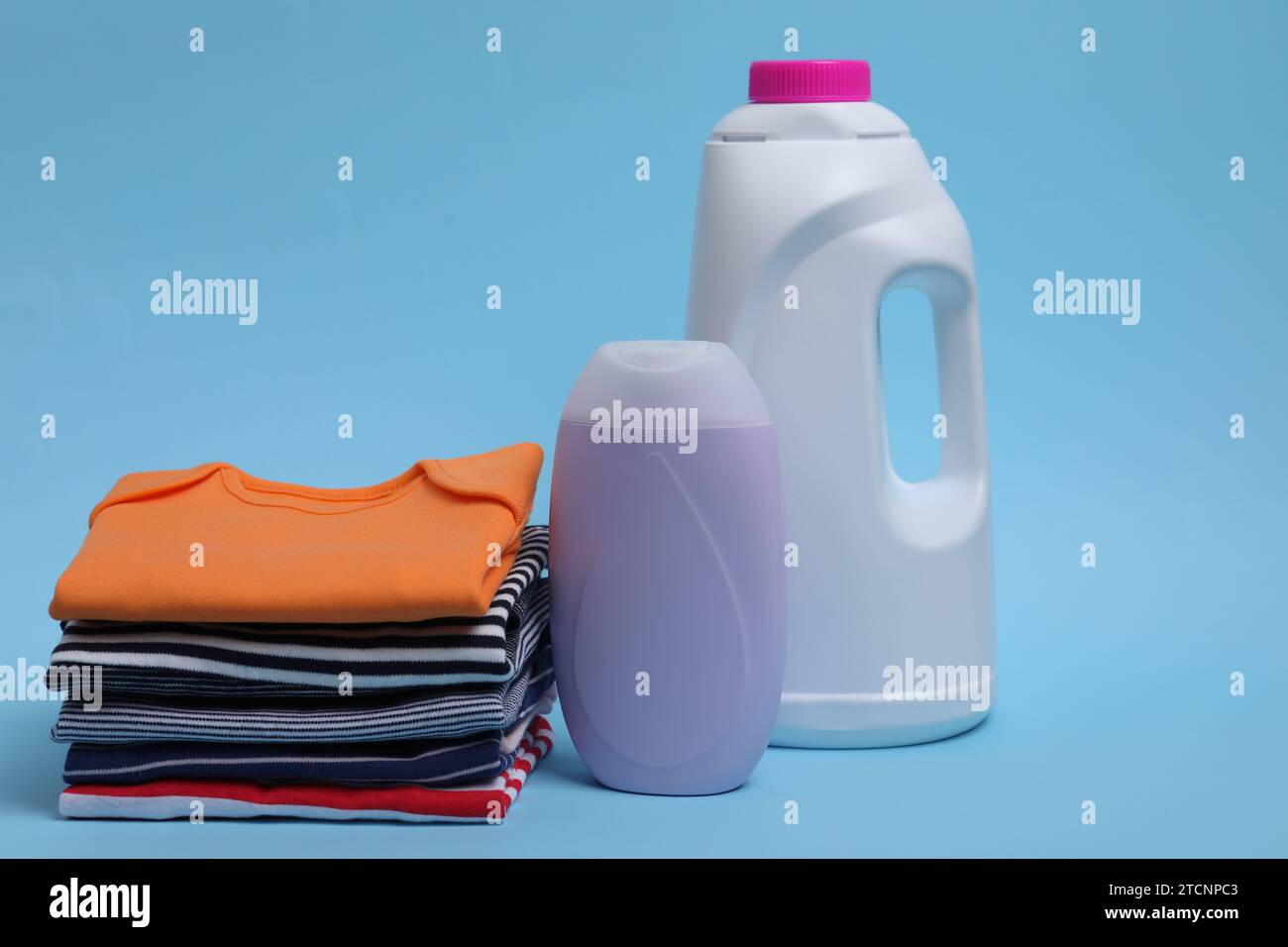 Stack of baby clothes and laundry detergents on light blue background ...