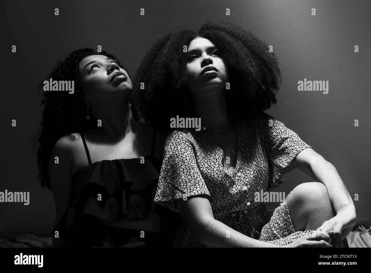 Black and white portrait of two young, beautiful female friends sitting, looking up. Studio low ...