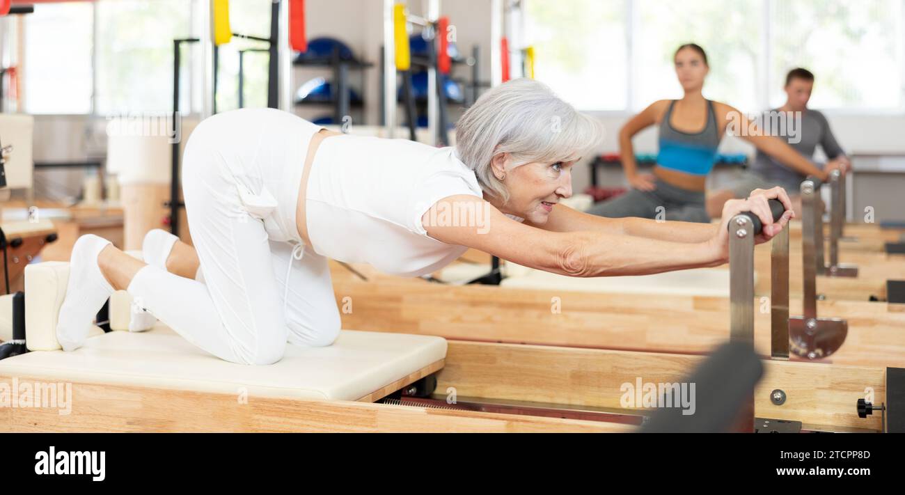Senior woman performs exercise on reformer to improve coordination ...