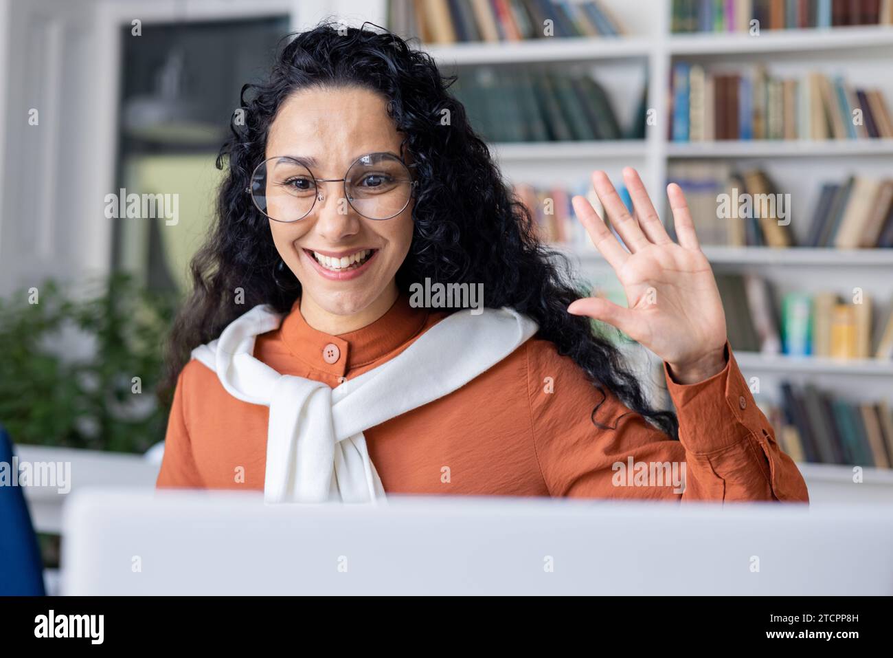 Happy hispanic female teacher conducts online class in office, waves at ...