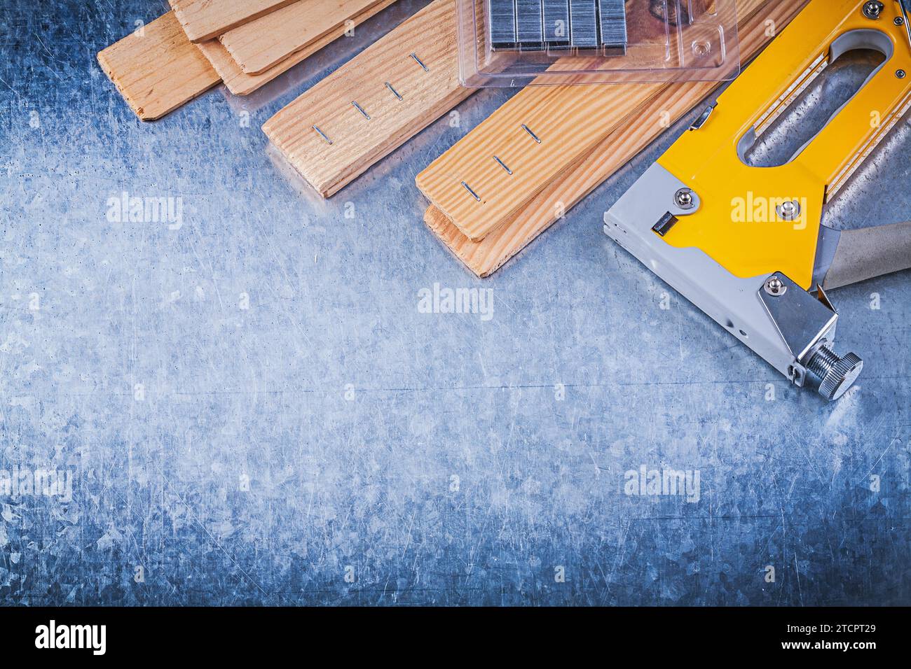 Yellow chrome staple gun staples wooden boards on a metallic background ...