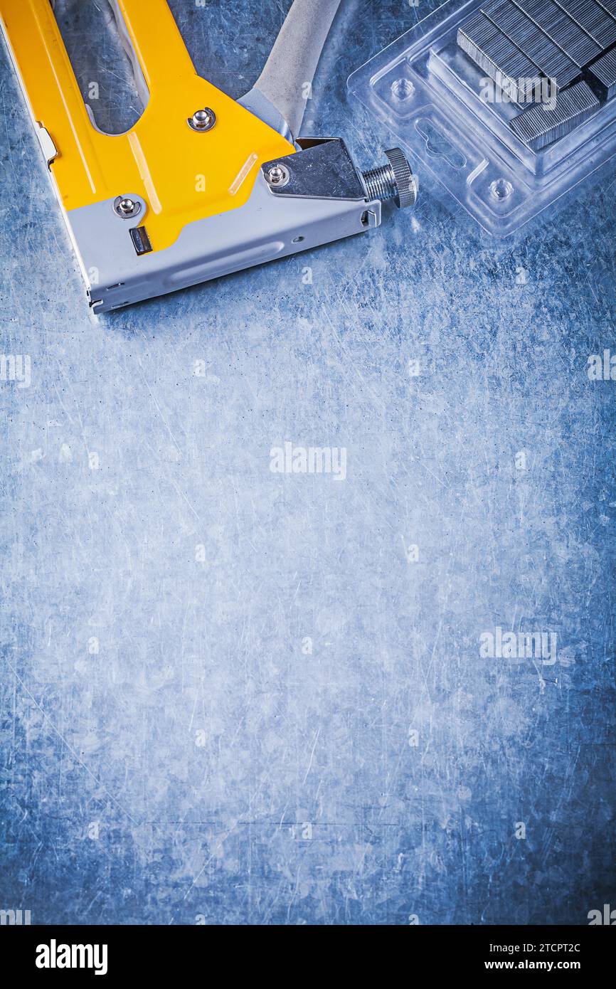 Yellow staple gun chrome staples on scratched metallic background ...