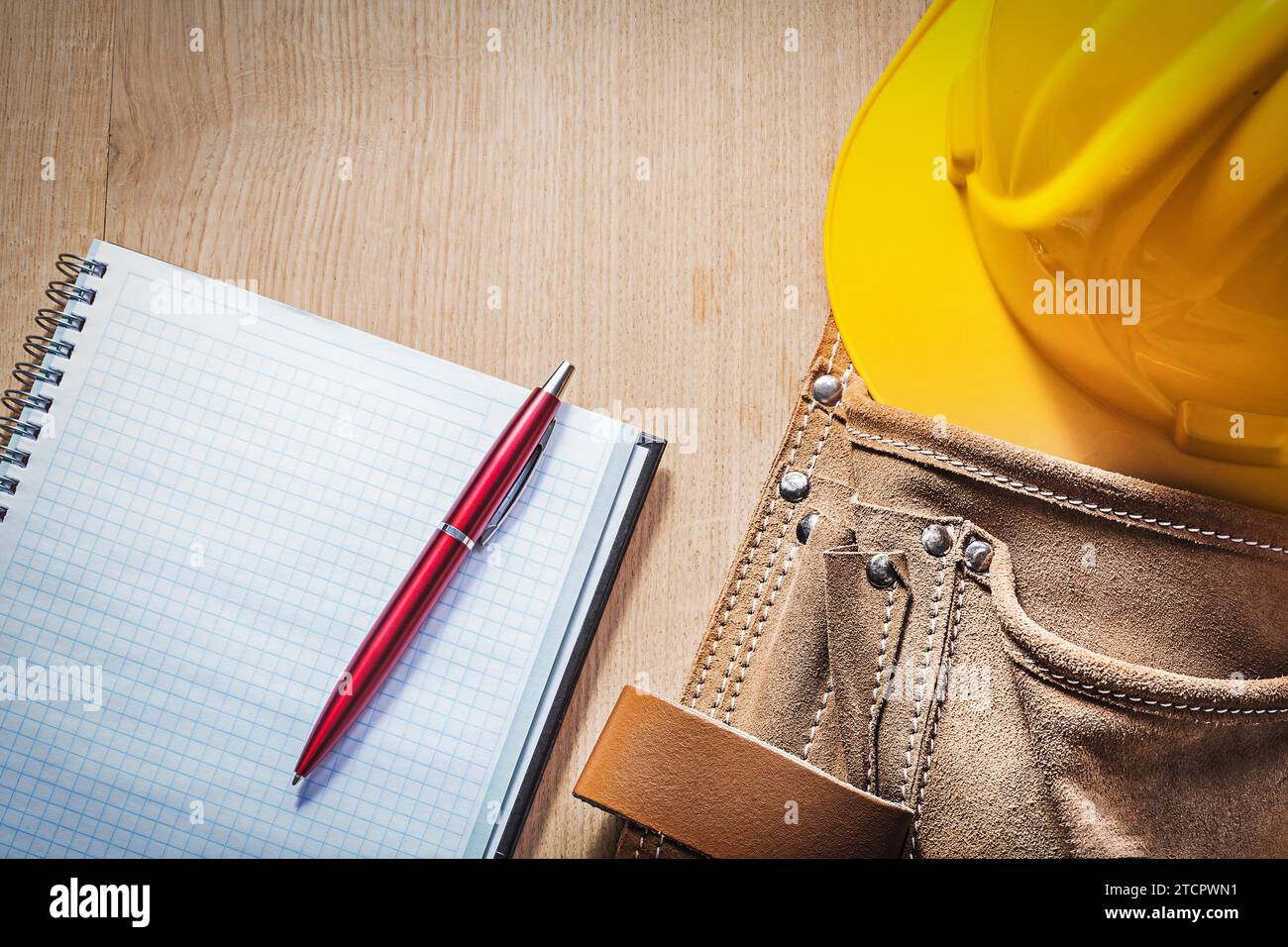 Leather tool belt, safety helmet, chequered notepad, pen on wooden ...
