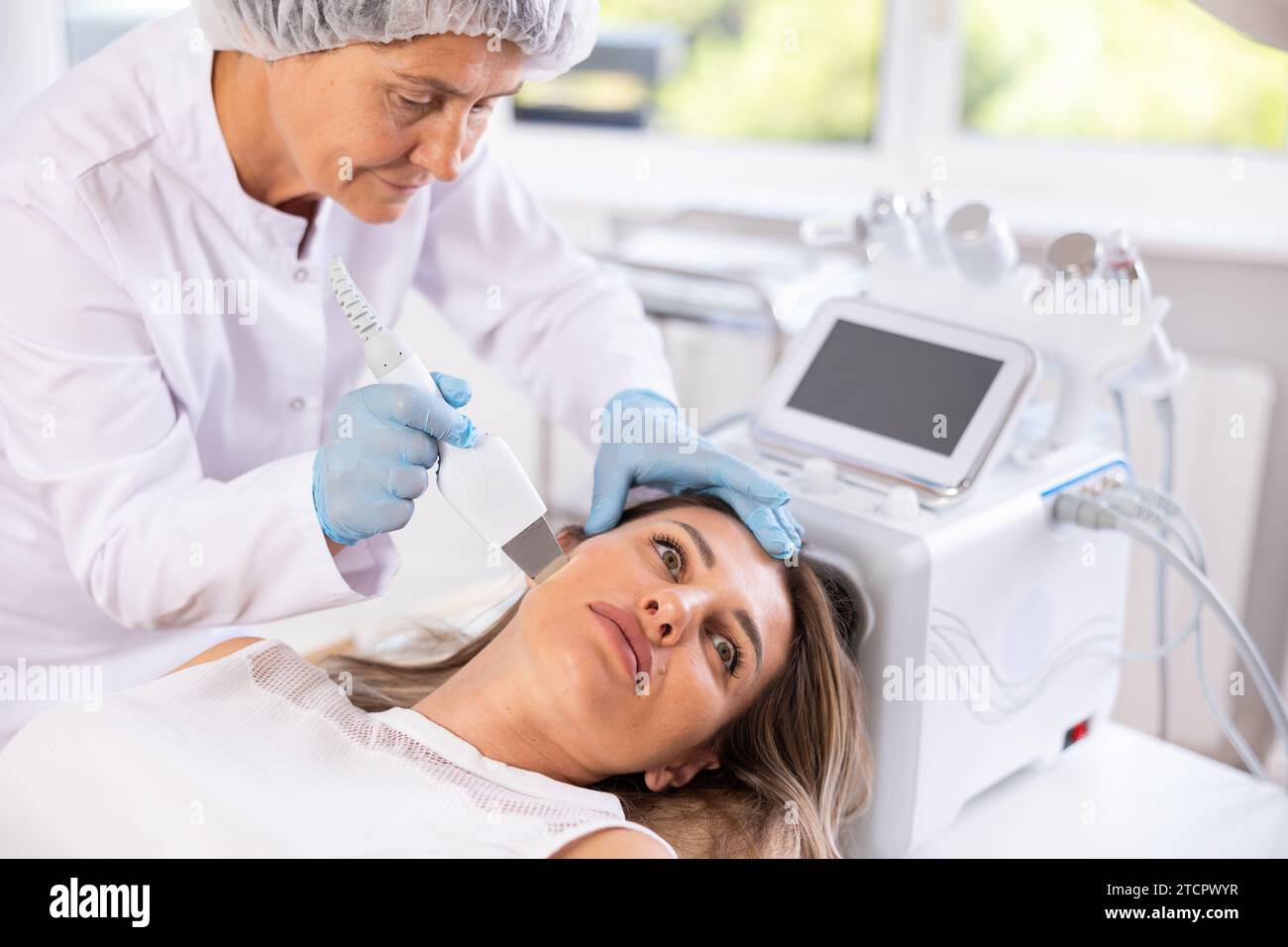 Young female client experiencing facial skin peeling with ultrasonic ...