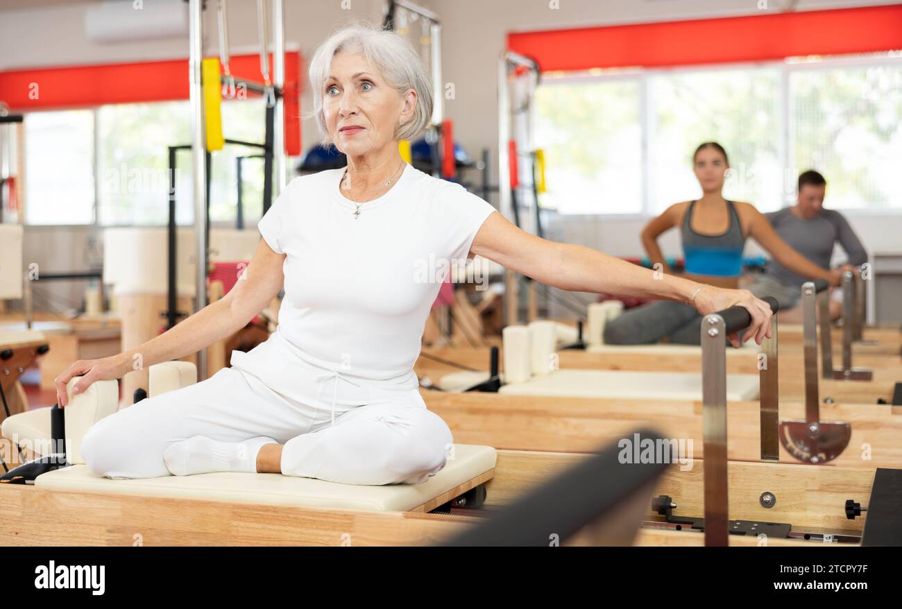 Senior woman performs exercise on reformer to improve coordination ...