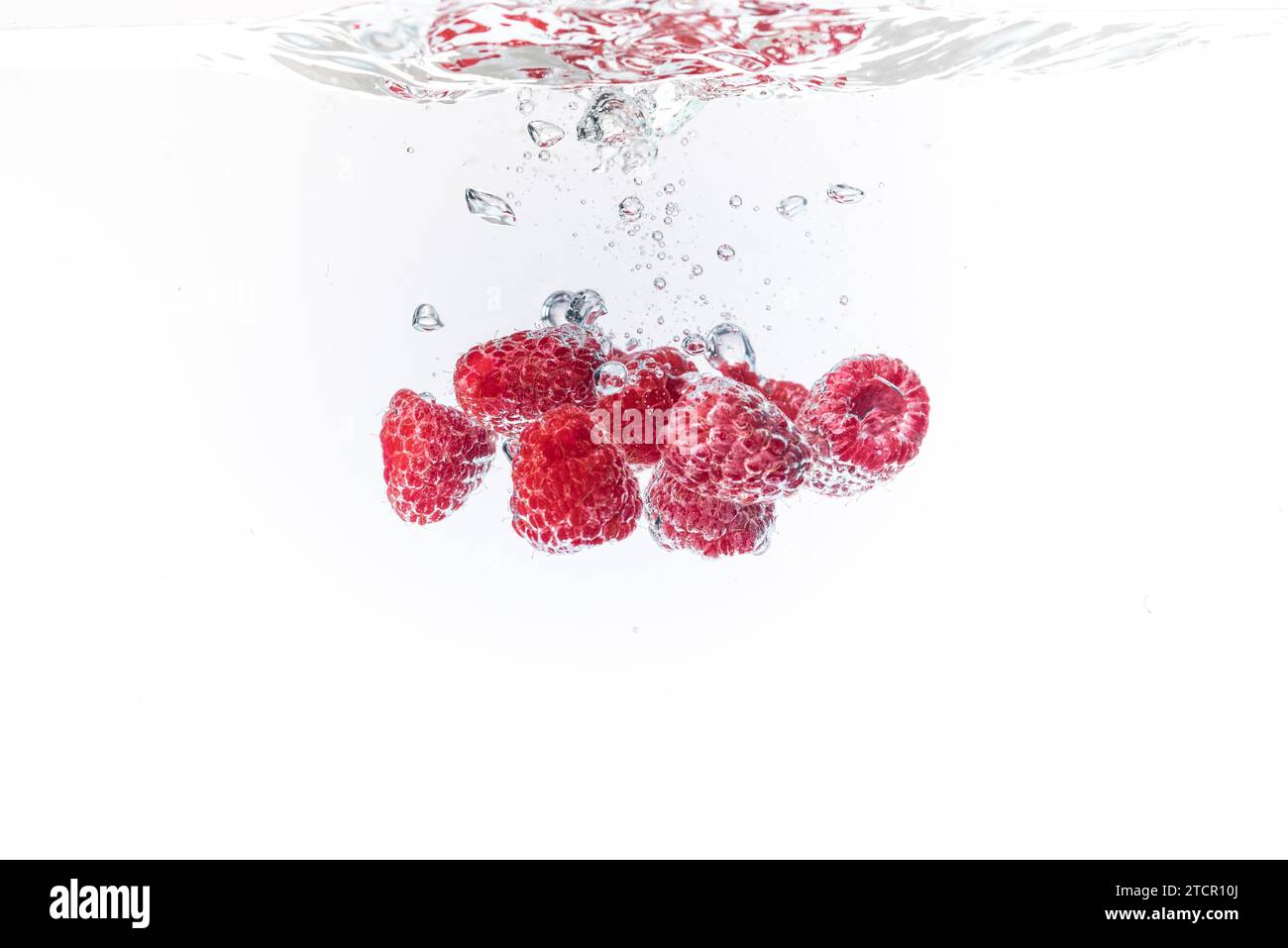 Raspberries splashing into crystal clear water with air bubbles ...