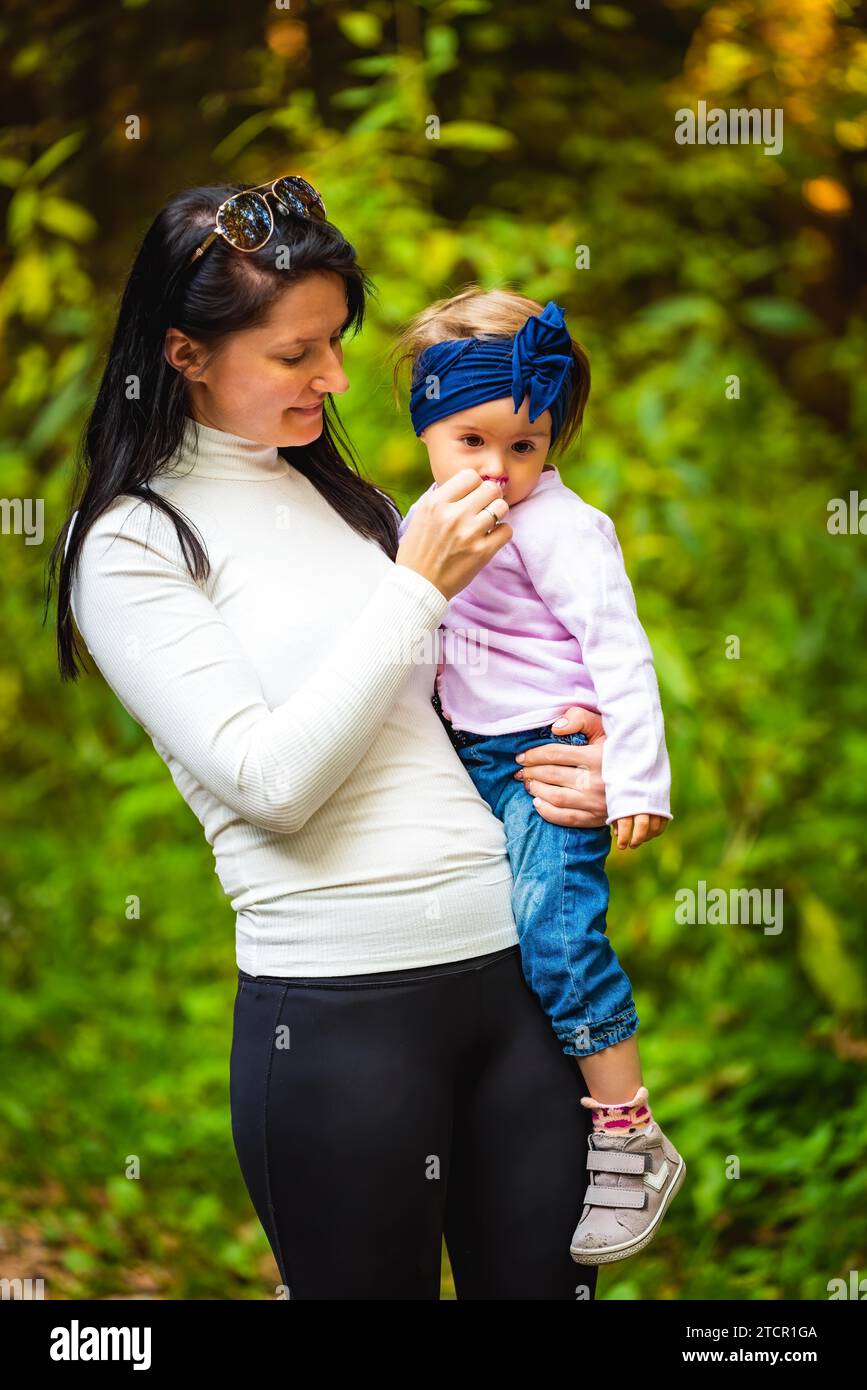 Mother holding baby girl sniffing a flower in forest. Childhood concept ...