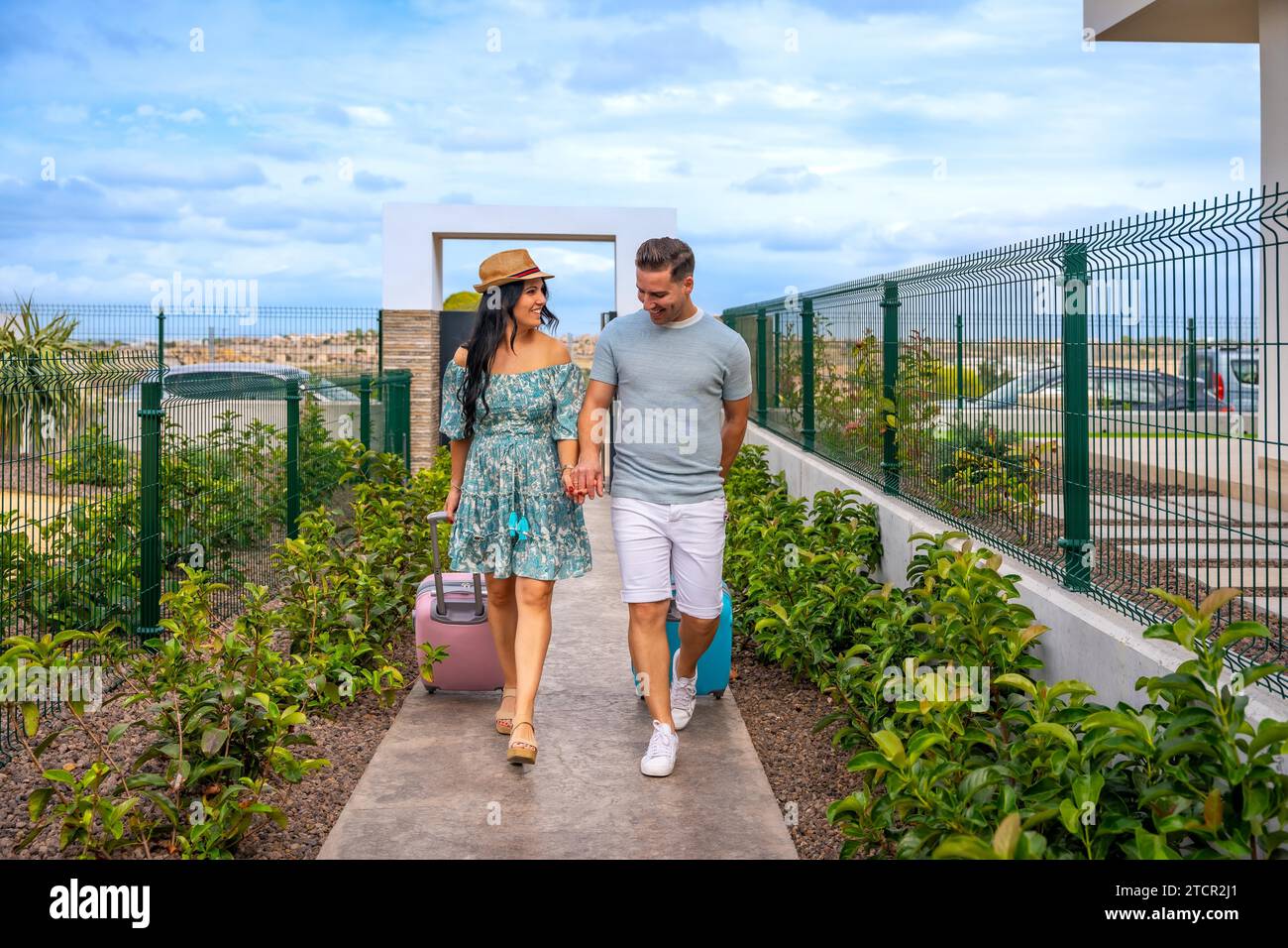 Frontal view of a couple holding hands carrying luggage while arriving ...