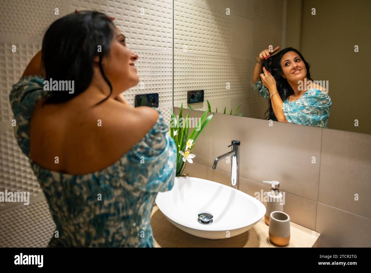 Woman facing the mirror and combing her hair alone in the bathroom at ...