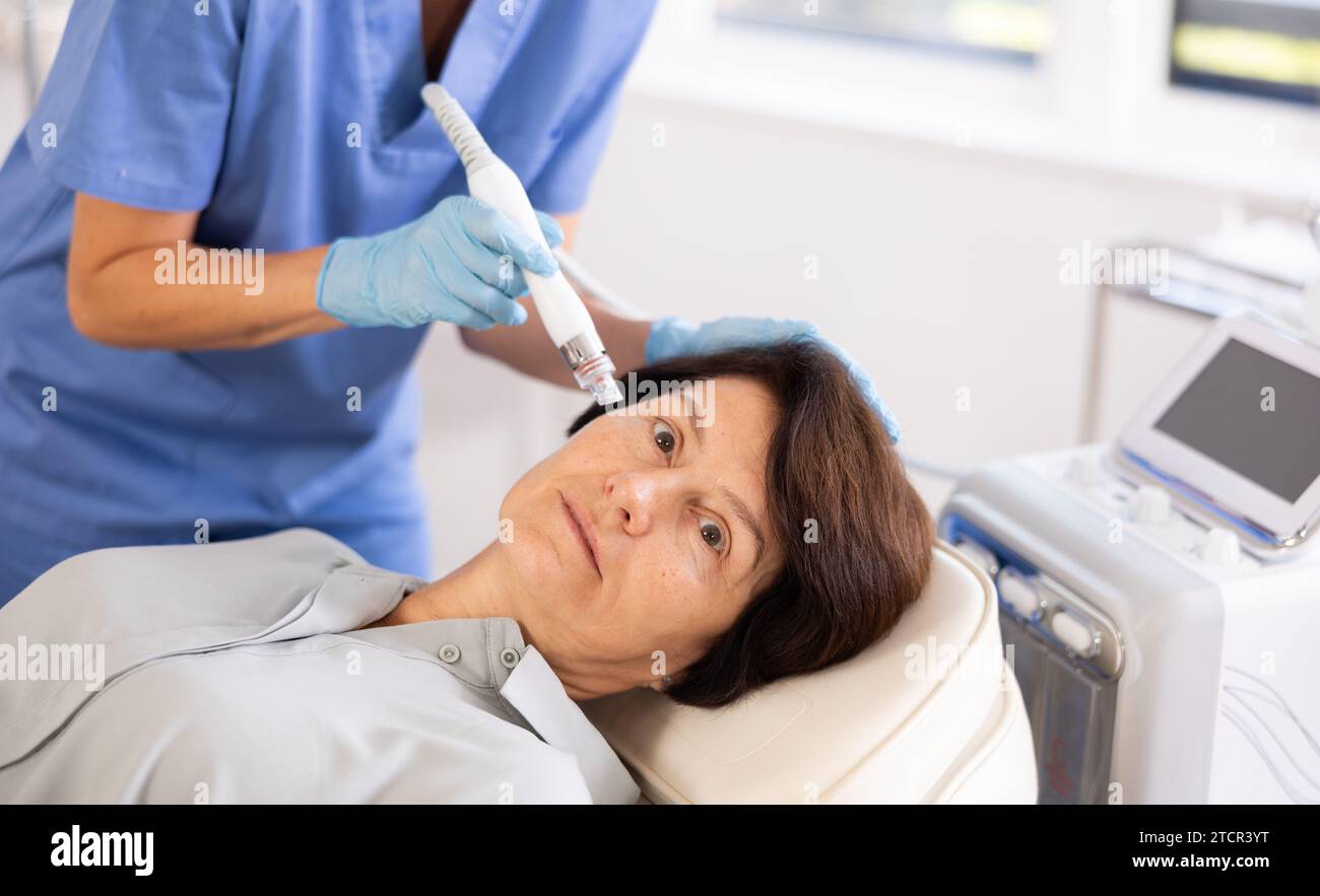 Aged woman undergoing cosmetic facial treatment using ion bubble ...