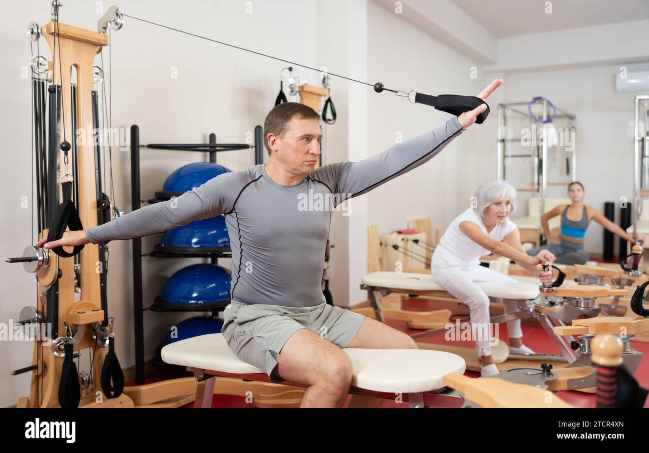Sports club man client on reformer with cable and rope performs ...