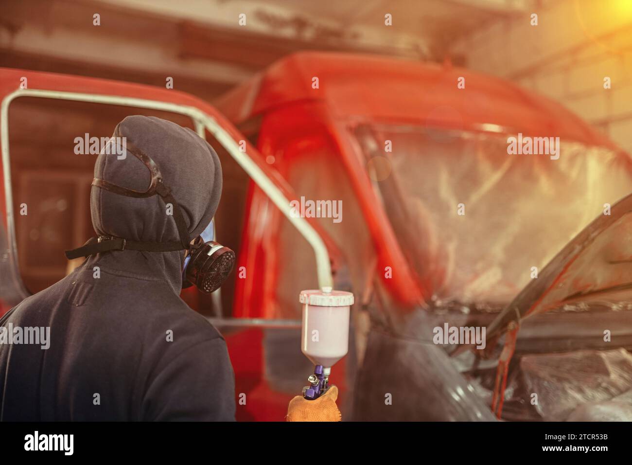 Body repair of a van, painting the body red, a mechanic in a respirator ...