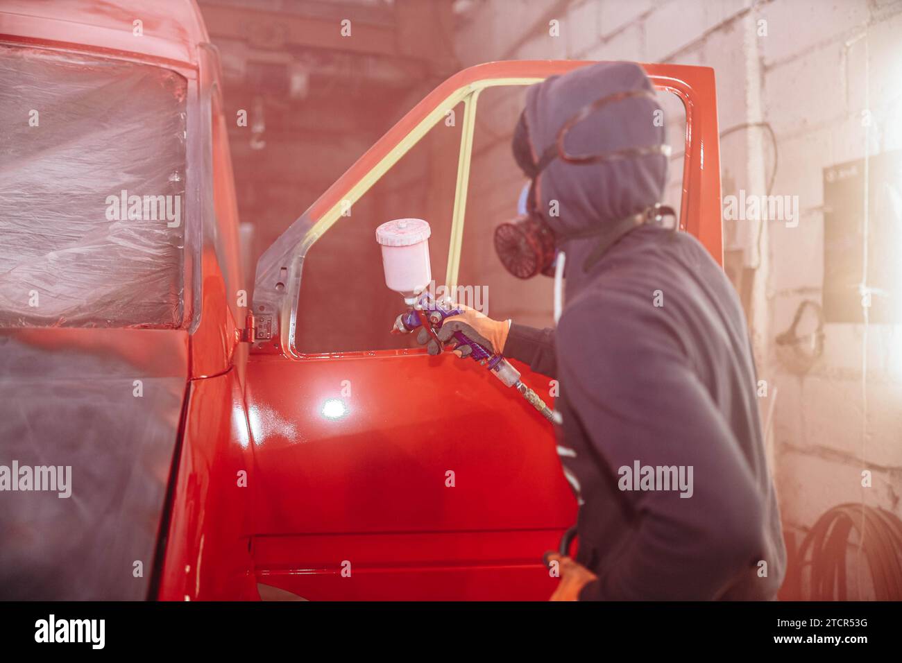 Body repair of a van, painting the body red, a mechanic in a respirator ...