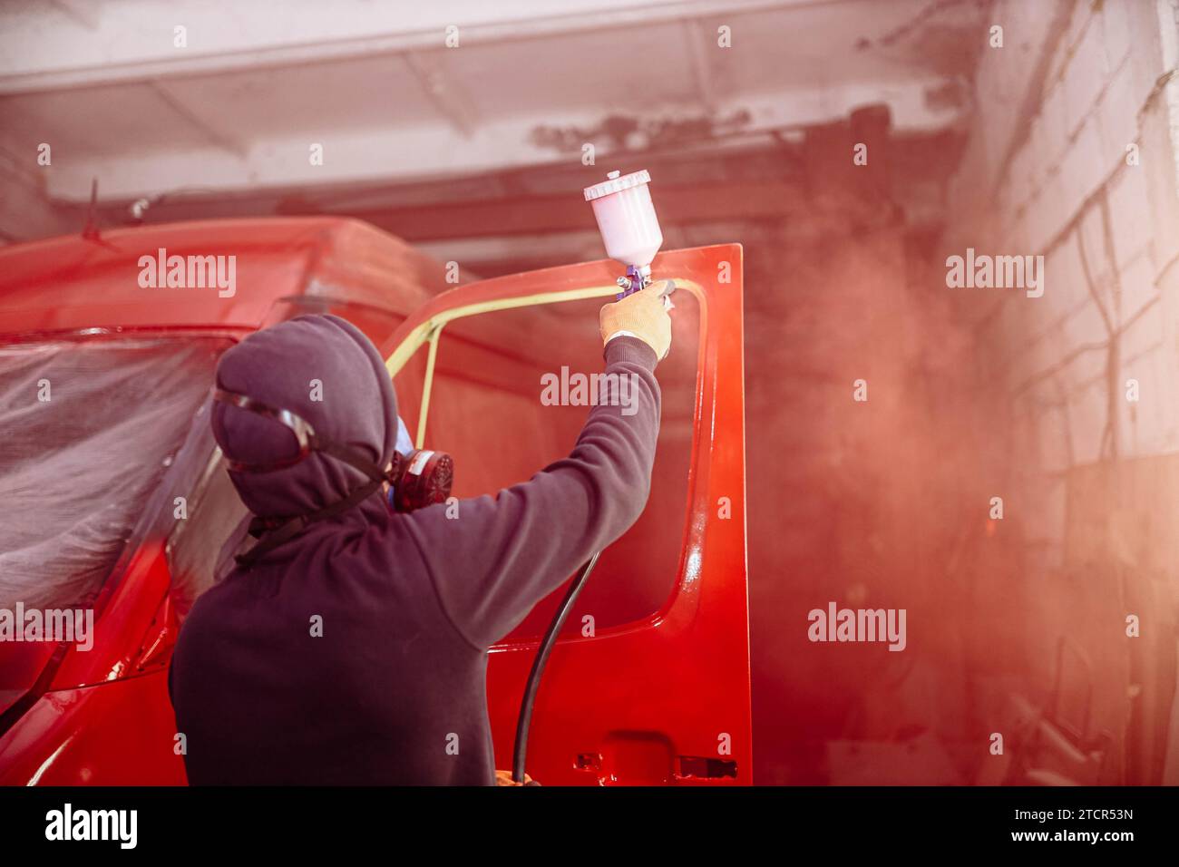 Body repair of a van, painting the body red, a mechanic in a respirator ...