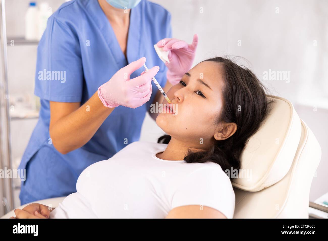 Face of young female client receiving injections during lip enhancement ...