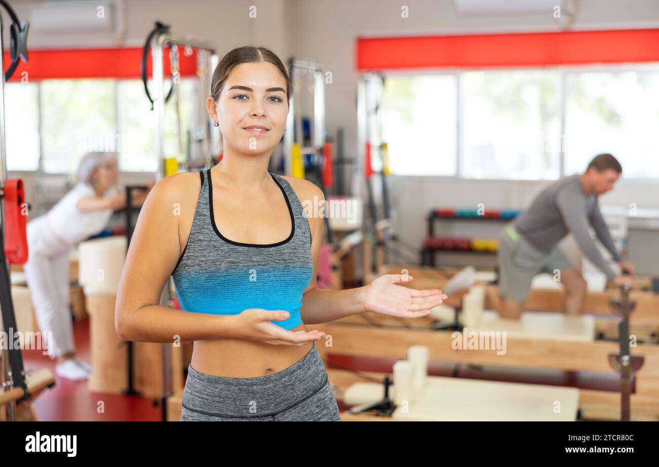 Positive girl coach stands in large gym against background of Pilates ...