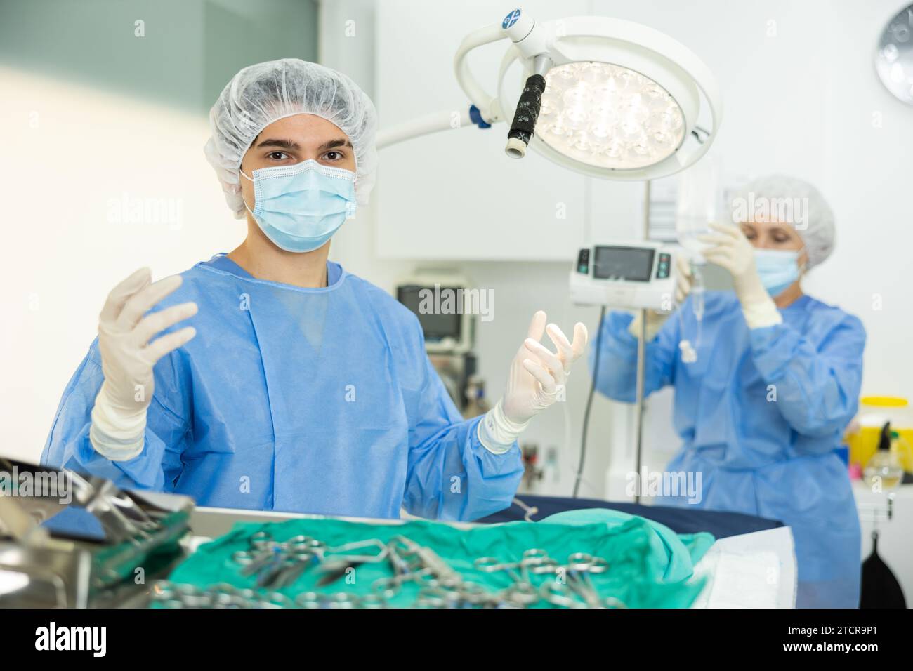 Man doctor stand with raised hands in gloves, female assistant pushes ...