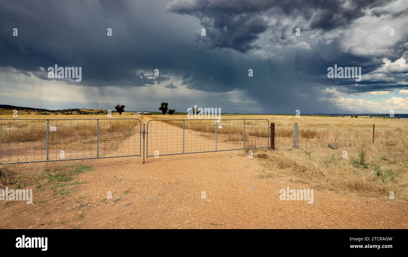 A wide gateway on farmland wide rain falling from dark clouds above at ...