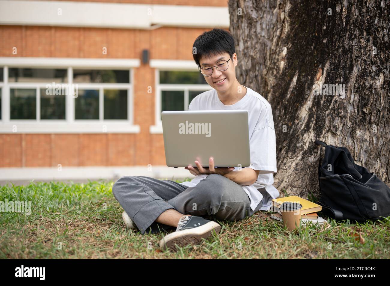 Young nerd and positive Asian male college student is using his laptop ...