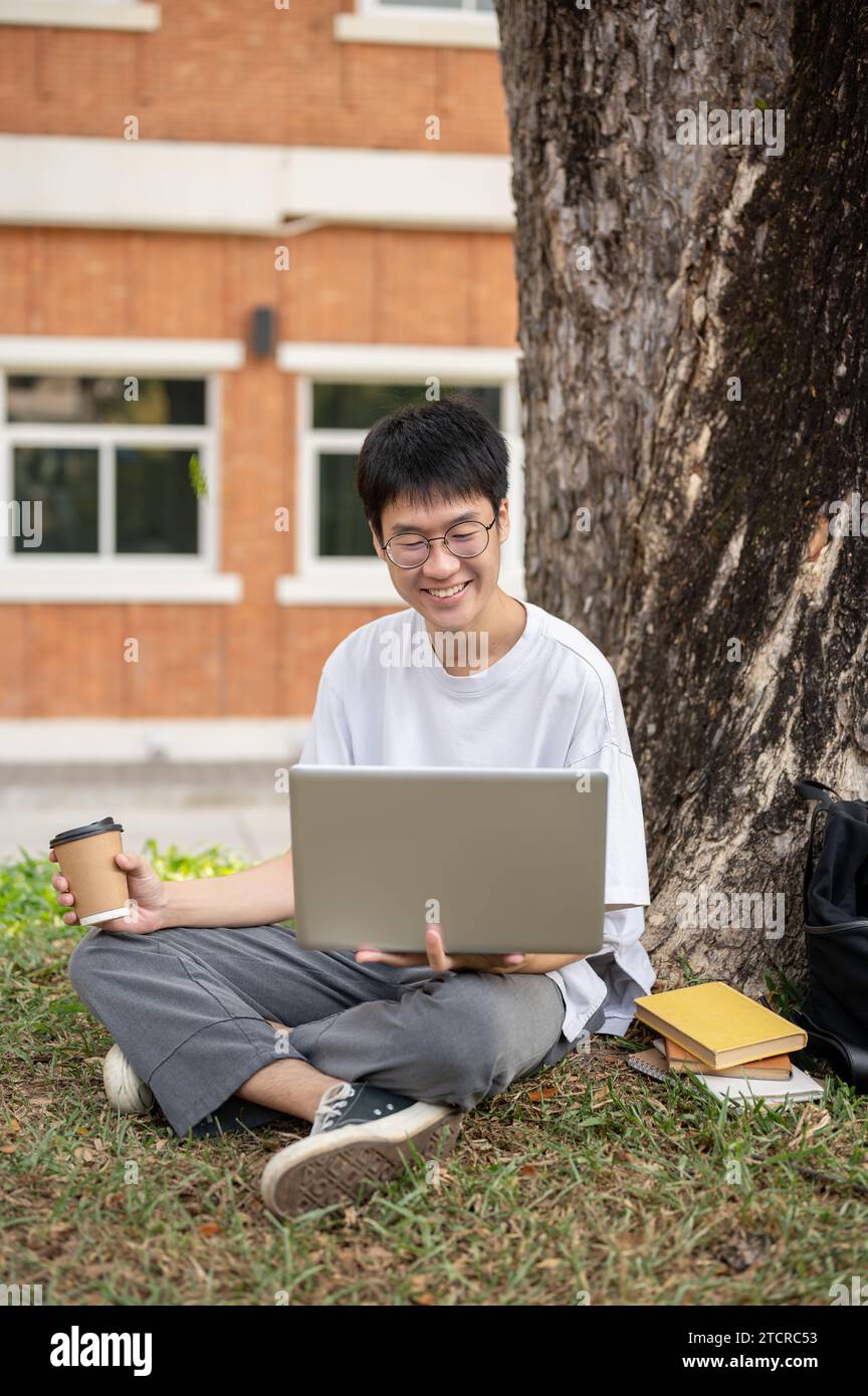 Young positive Asian male college student is using his laptop computer ...