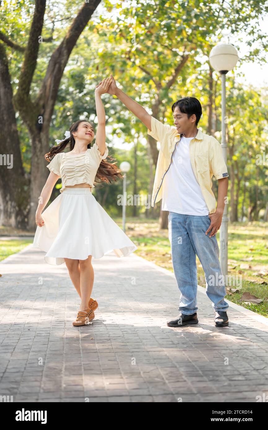 A lovely young Asian couple is dancing in a beautiful green park ...