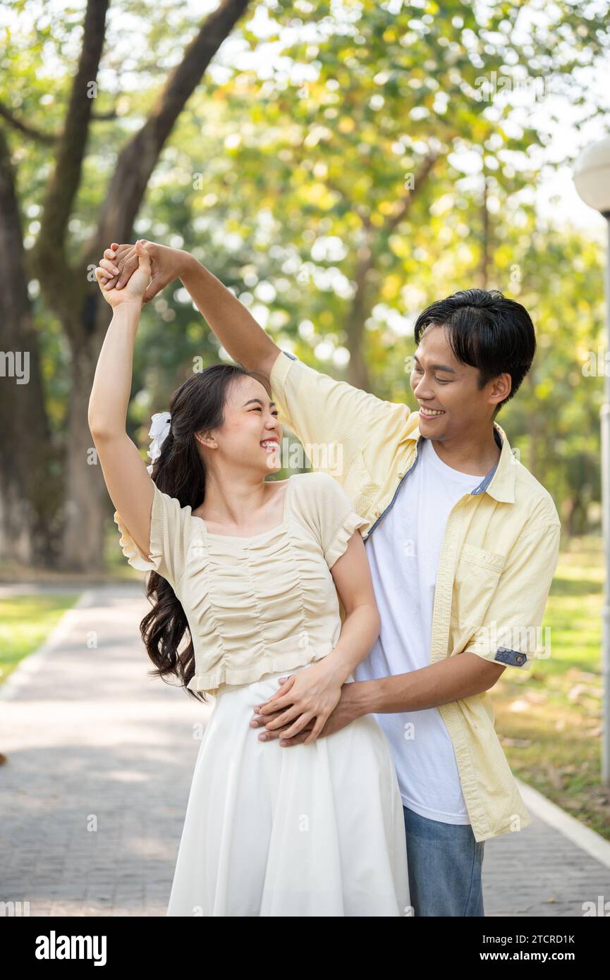 A lovely young Asian couple is dancing in a beautiful green park ...